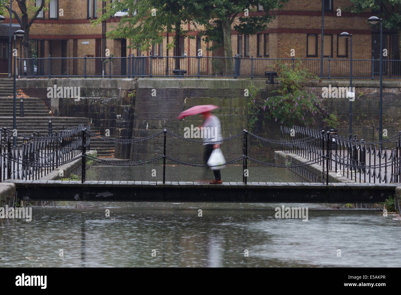 Man holding red umbrella in torrential rain crossing bridge over ...