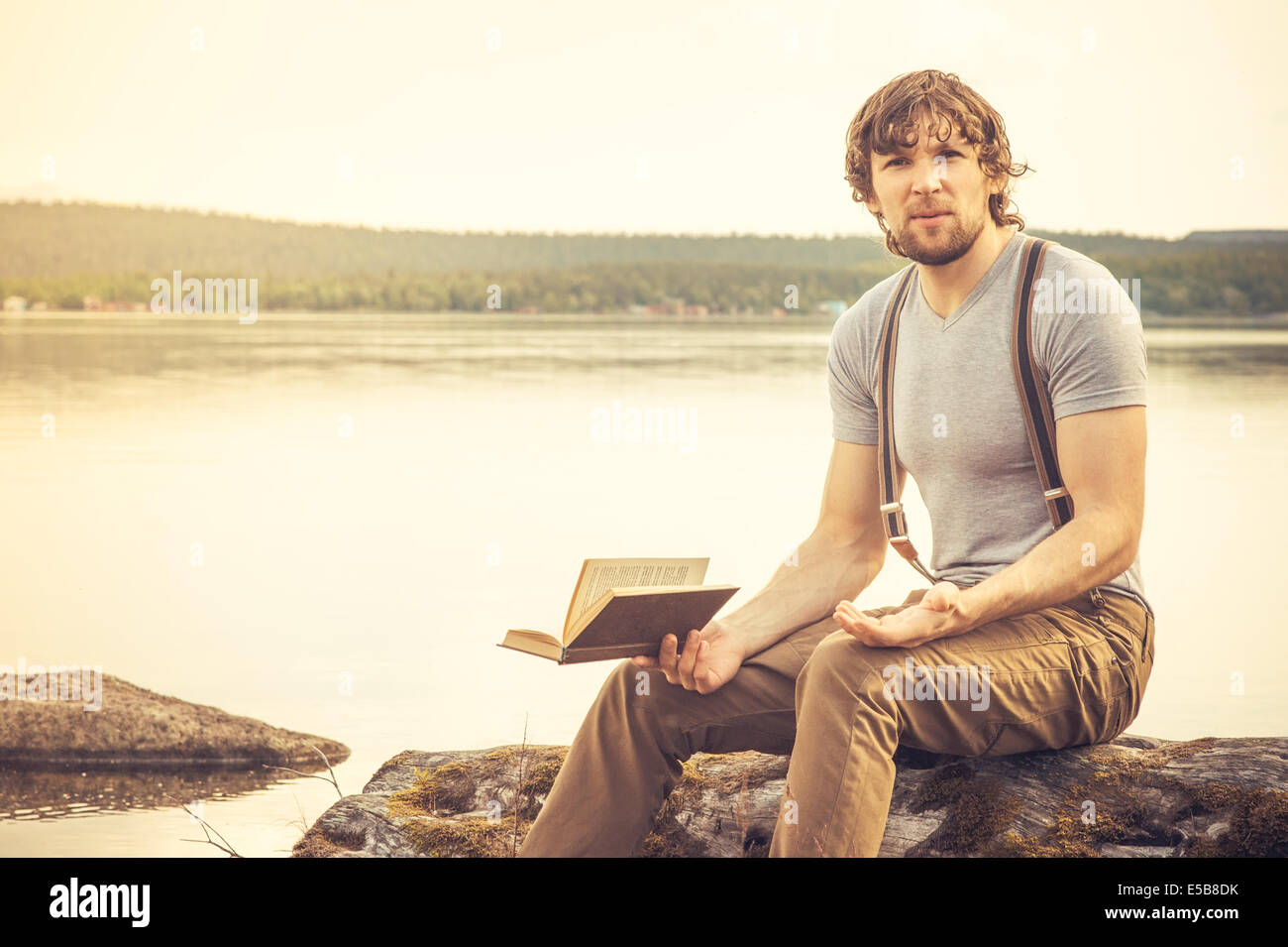Young Man reading book outdoor with lake on background Summer vacations ...