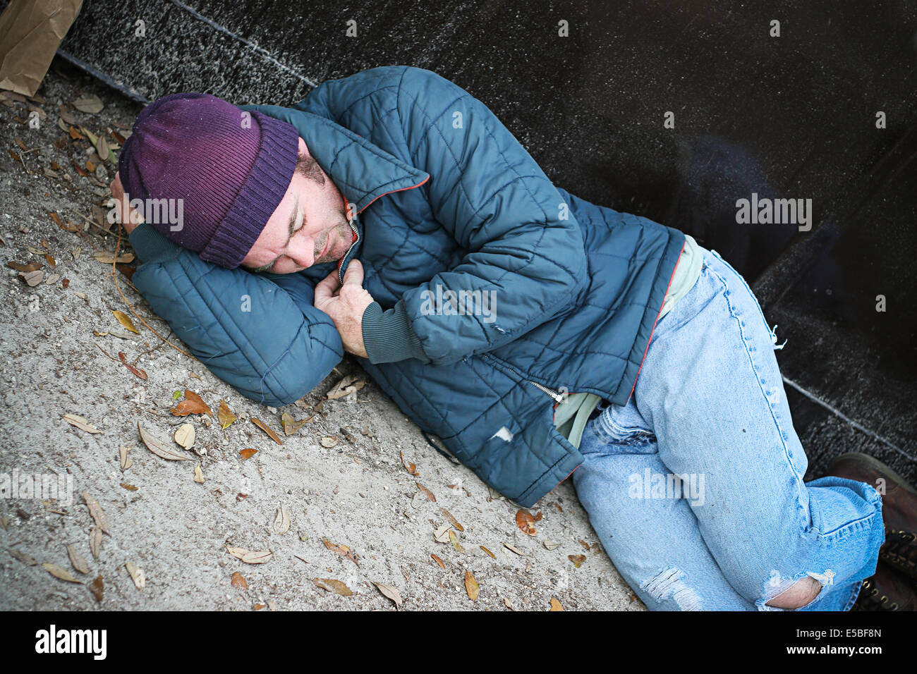 Homeless man cold and along trying to sleep on the ground beside a ...