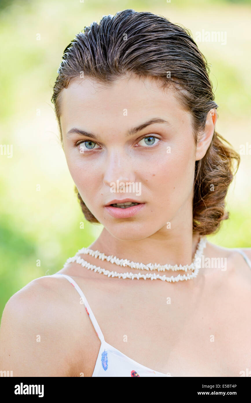 Portrait of a young woman smiling in the park, with summer back light and trees in the ...
