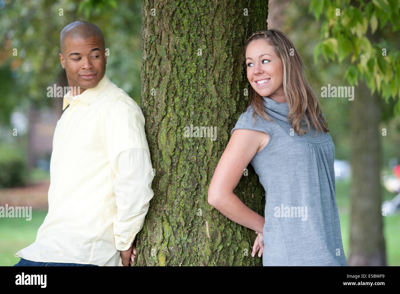A happy young interracial couple posing next to a tree on a sunny day ...