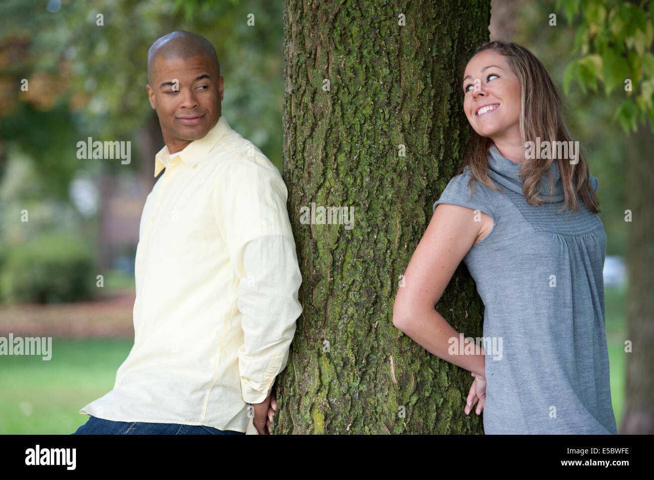 A happy young interracial couple posing next to a tree on a sunny day ...
