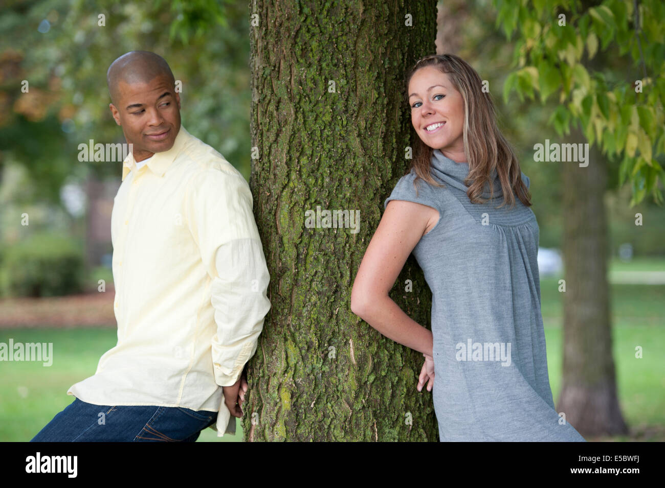 A happy young interracial couple posing next to a tree on a sunny day ...