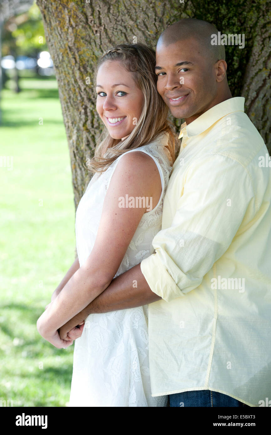 A happy and young Interracial couple posing on a sunny day under a tree ...