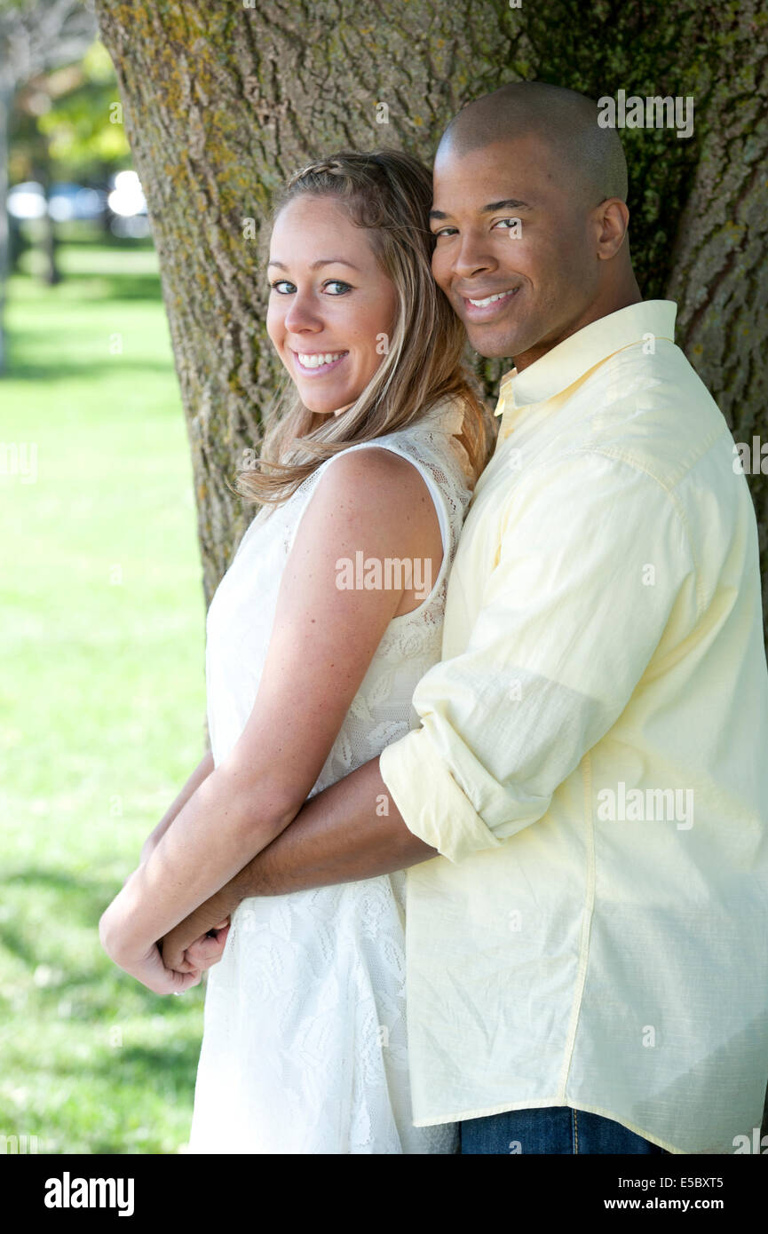A Happy And Young Interracial Couple Posing On A Sunny Day Under A Tree