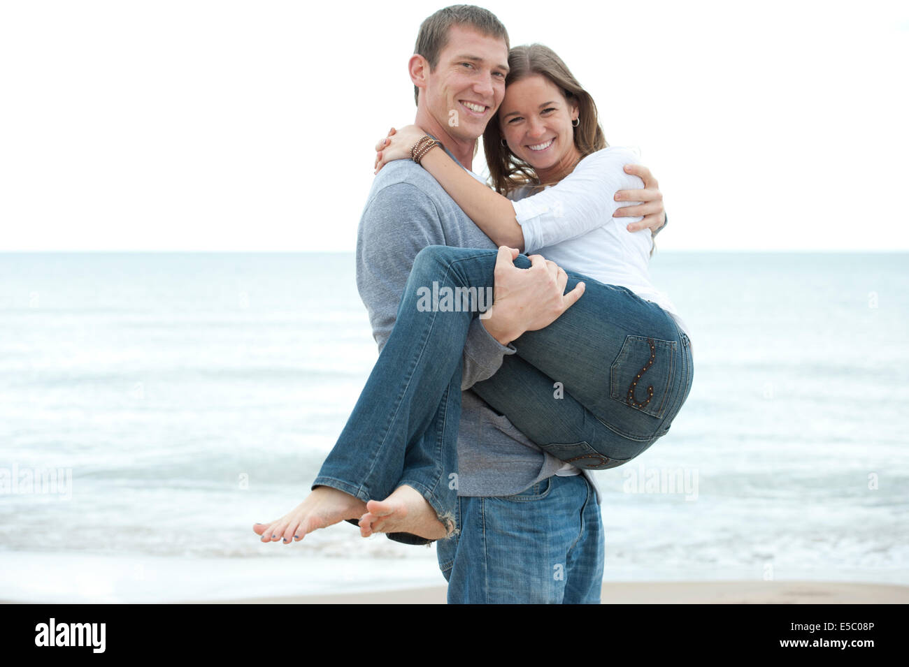 A young man carrying his wife smiling on the beach Stock Photo - Alamy