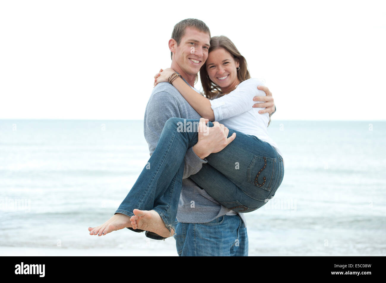 A young man carrying his wife smiling on the beach Stock Photo - Alamy