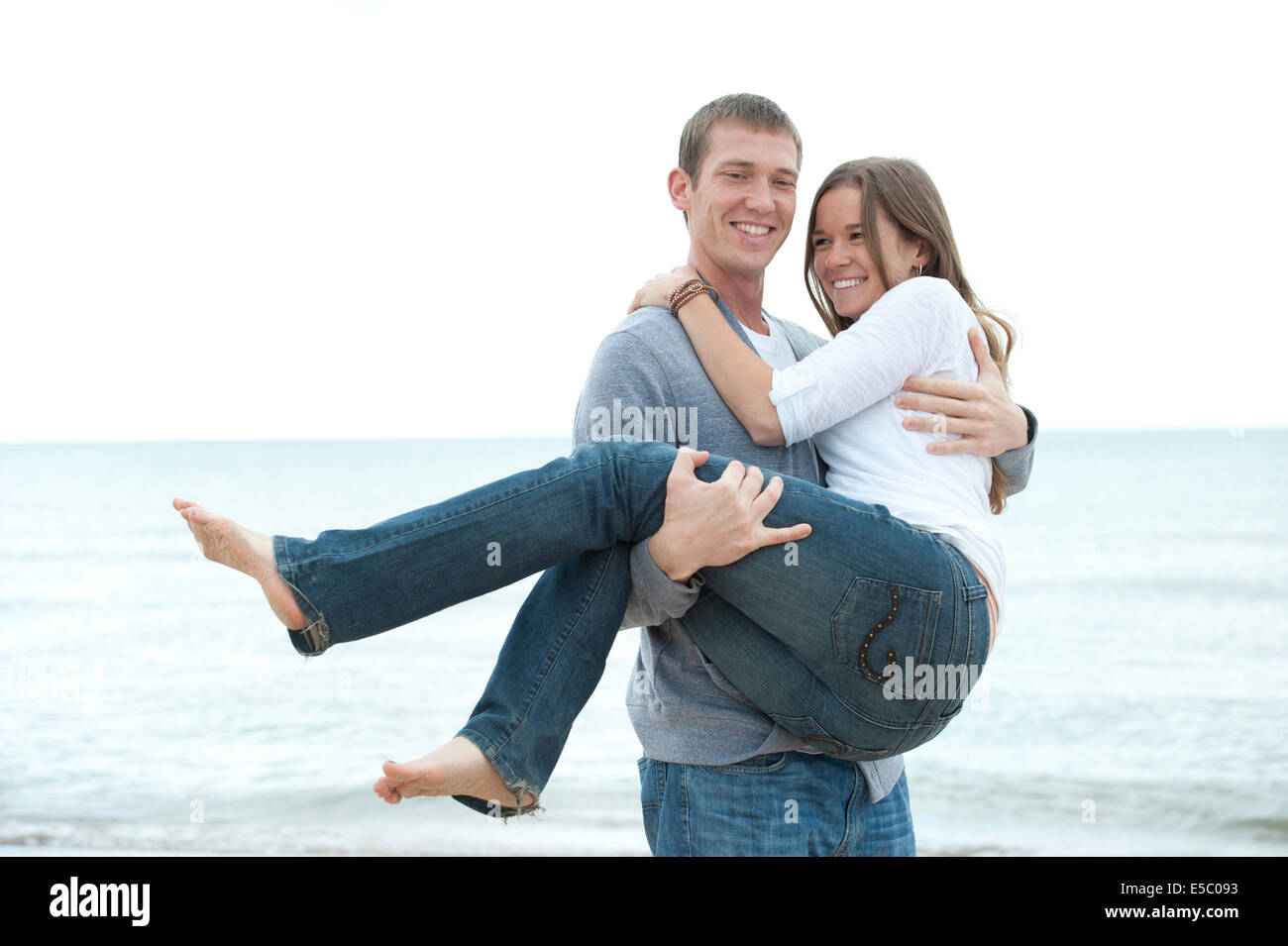 A young man carrying his wife smiling on the beach Stock Photo - Alamy