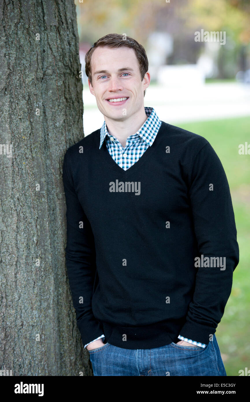 An attractive young male model posing by a tree wearing a sweater and a ...