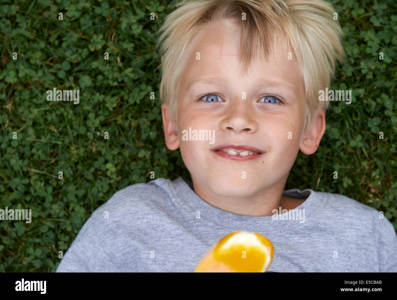 Blond child 6-8 year old boy holds, lickling and eating yellow ice ...