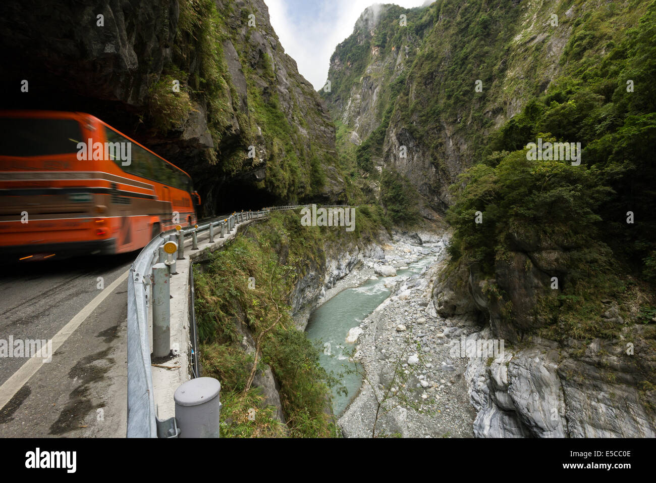 Bus on the road at the rugged and steep mountains next to rocky river ...