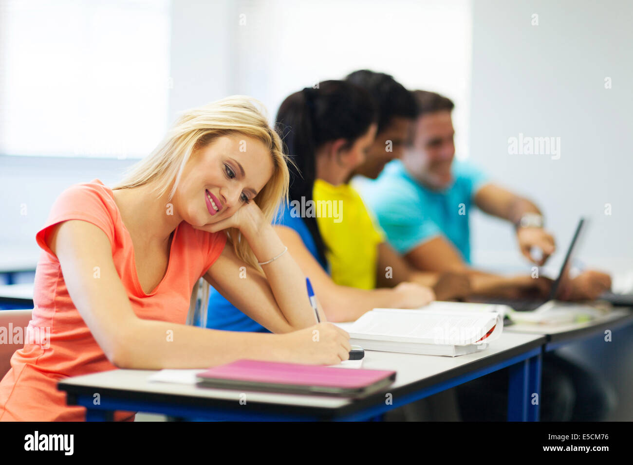 beautiful female student writing notes in classroom with classmates on ...