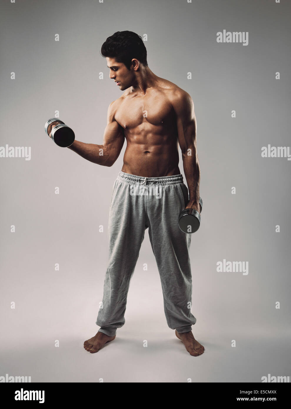 Full length portrait of muscular young man exercising with dumbbells on ...