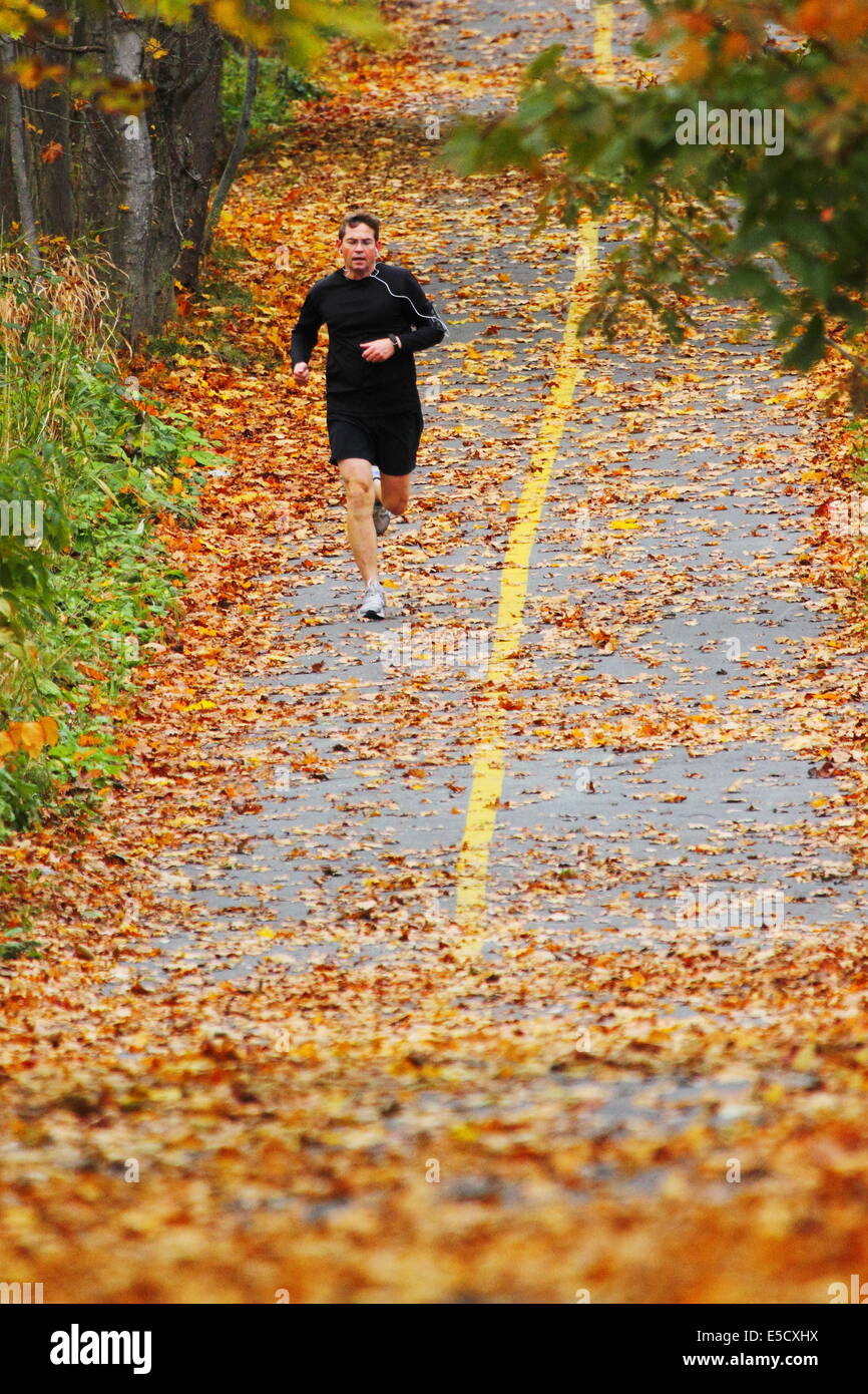 A male runner dressed in black jogs along a trail covered with fall ...