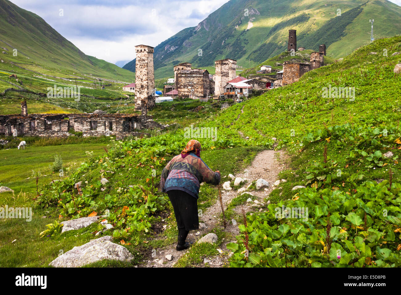 Old woman walking next to the koshki medieval towers of Ushguli ...