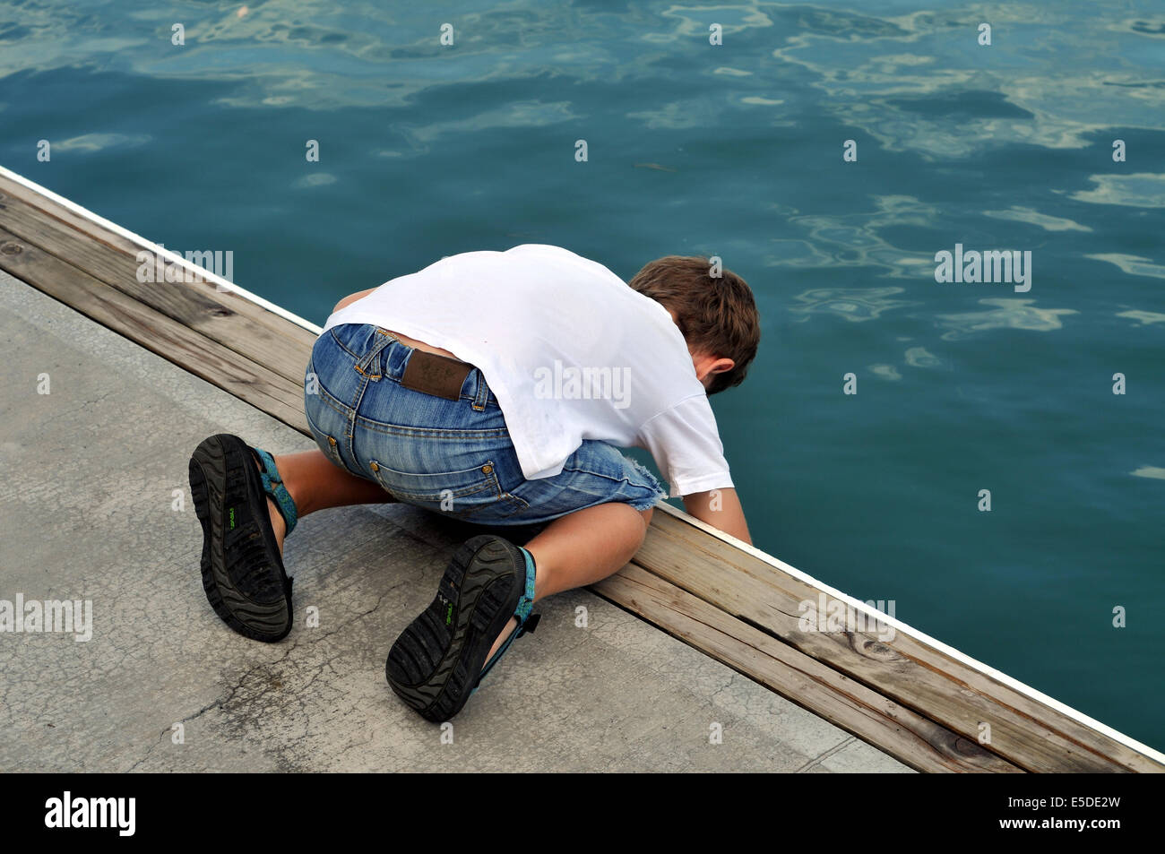Boy on wharf looking into water Stock Photo - Alamy
