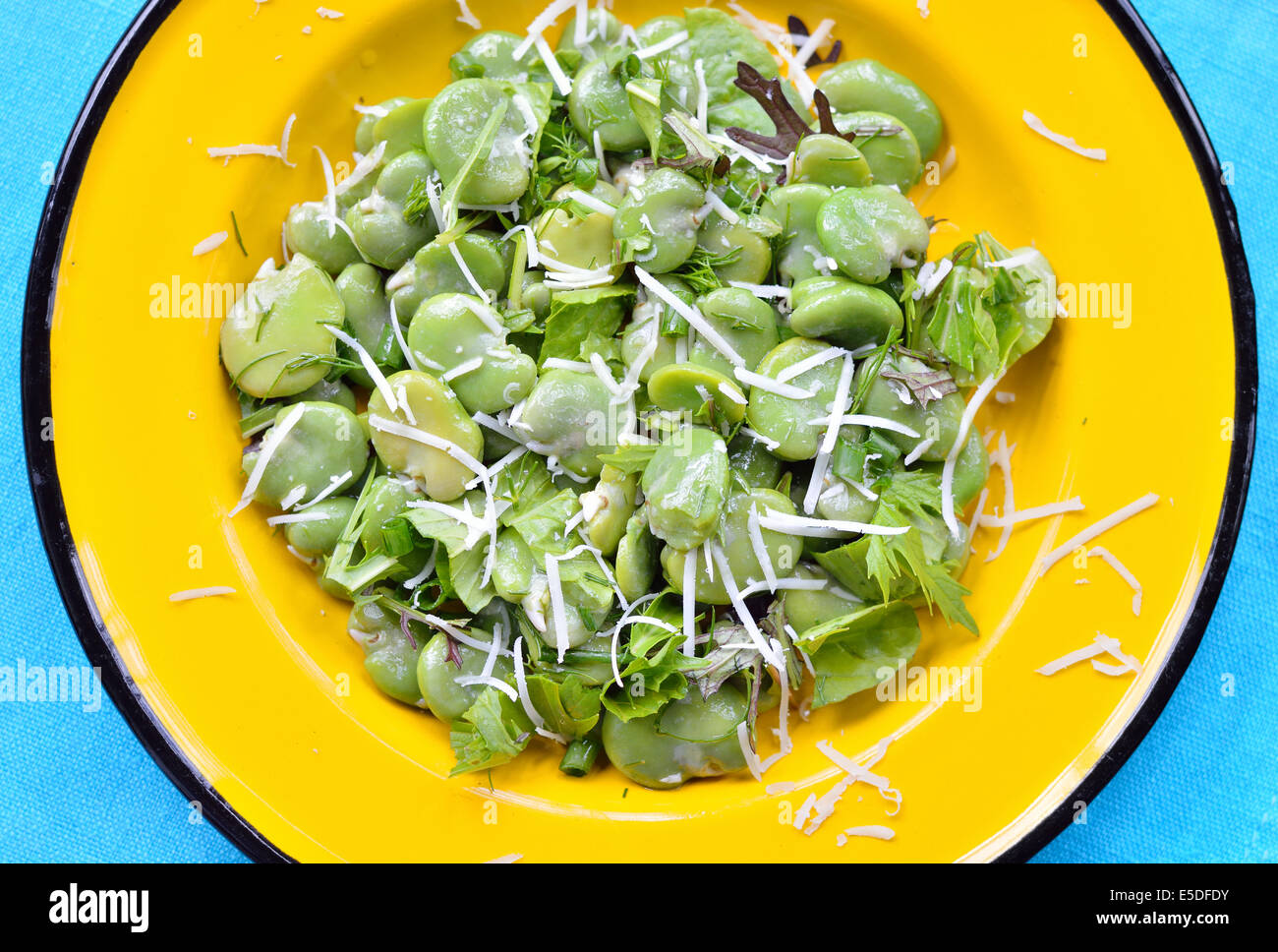 Green broad bean salad on yellow plate on blue tablecloth. Broad bean ...