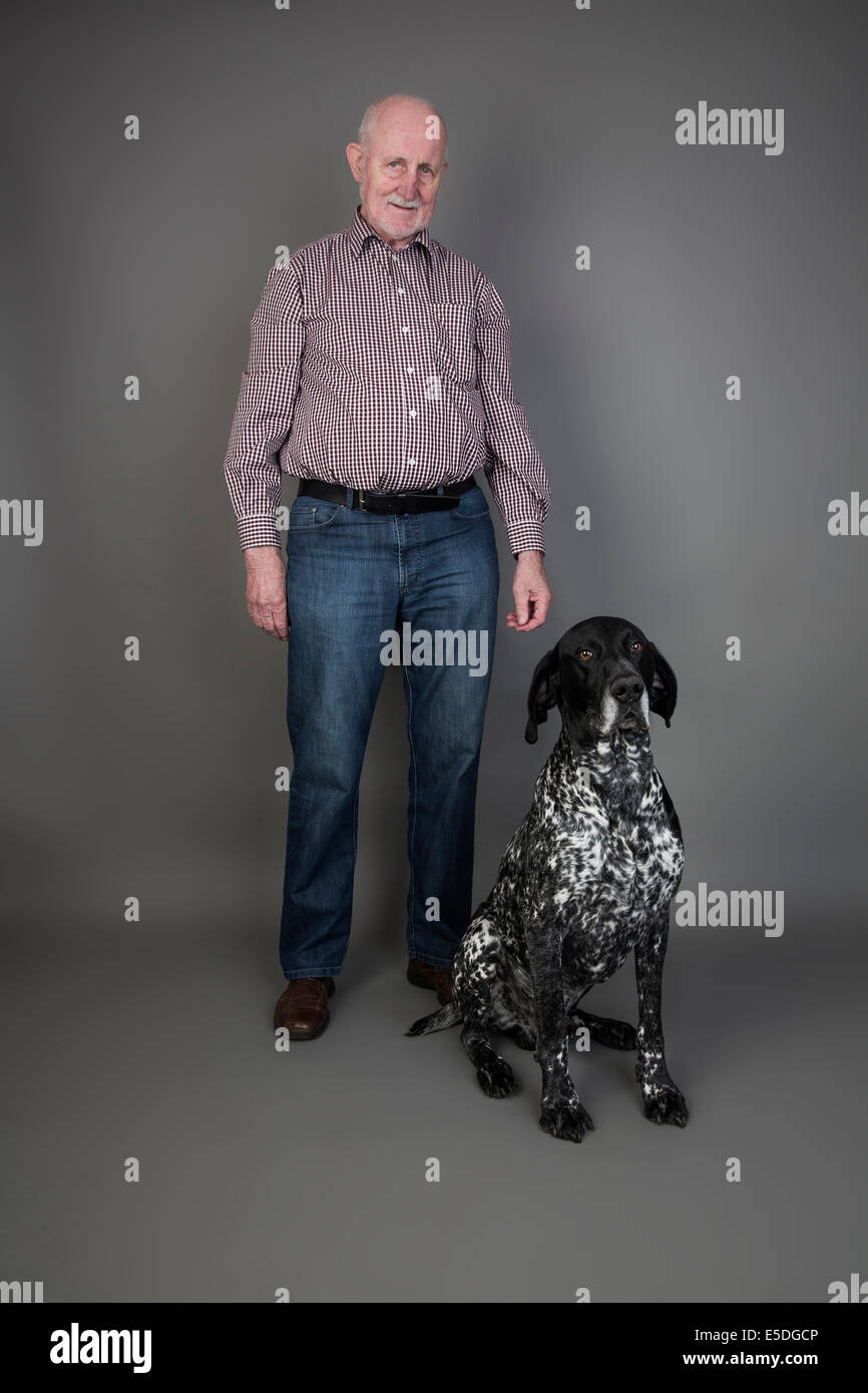 Senior man with his German Shorthaired Pointer in front of grey ...
