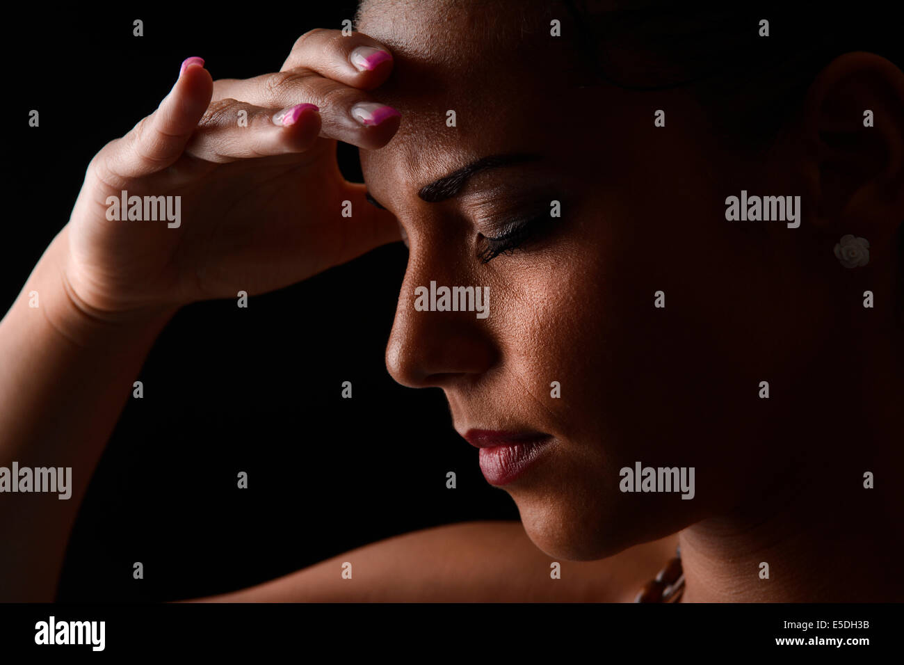 Portrait of young woman with hand on her forehead in front of black ...