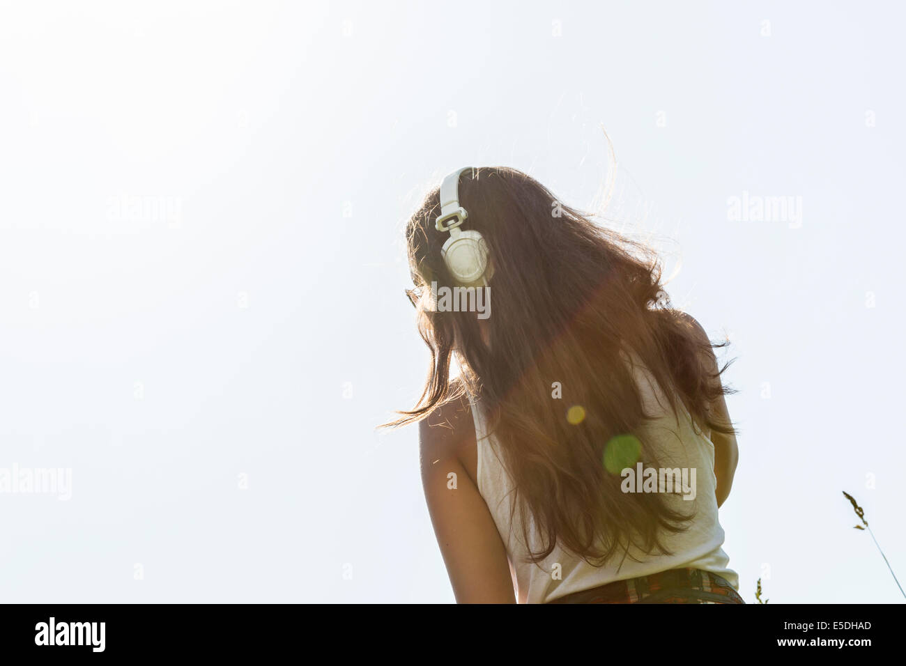 Young woman with headphones in front of sky, back view Stock Photo - Alamy