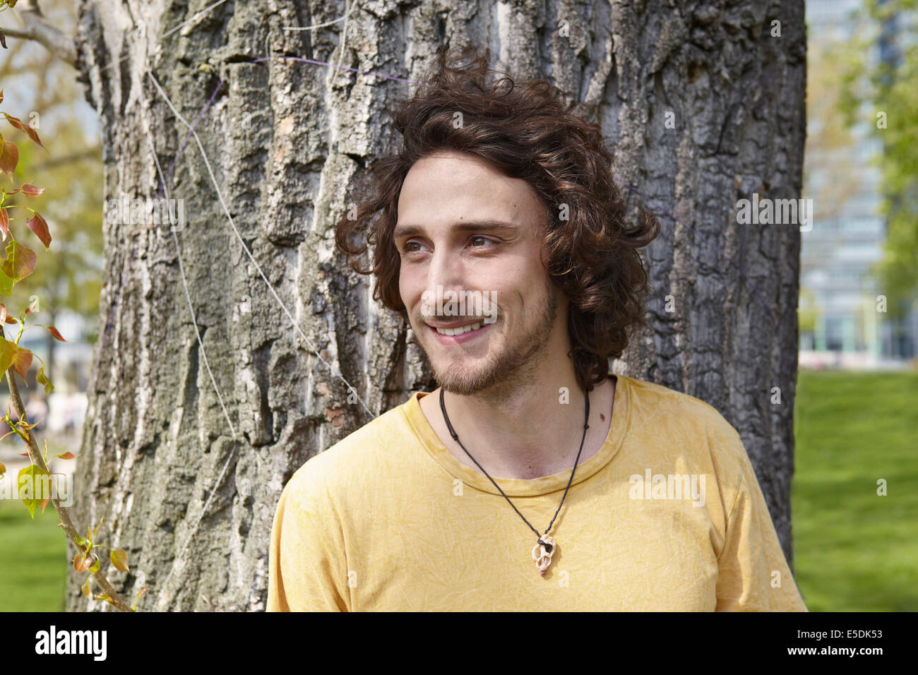 Smiling young man at tree trunk Stock Photo - Alamy