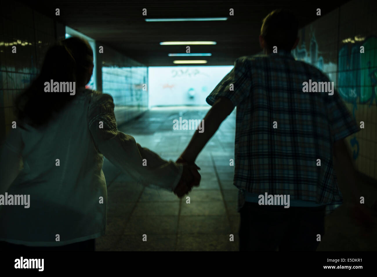Young couple running hand in hand in a dark underpass, back view Stock ...