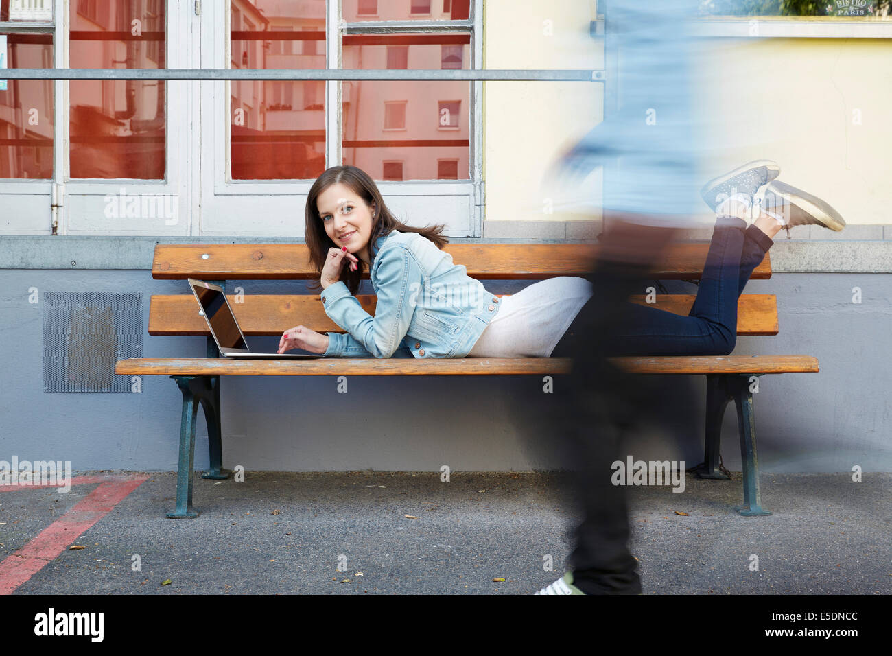 Woman with laptop lying on bench with person passing by Stock Photo - Alamy