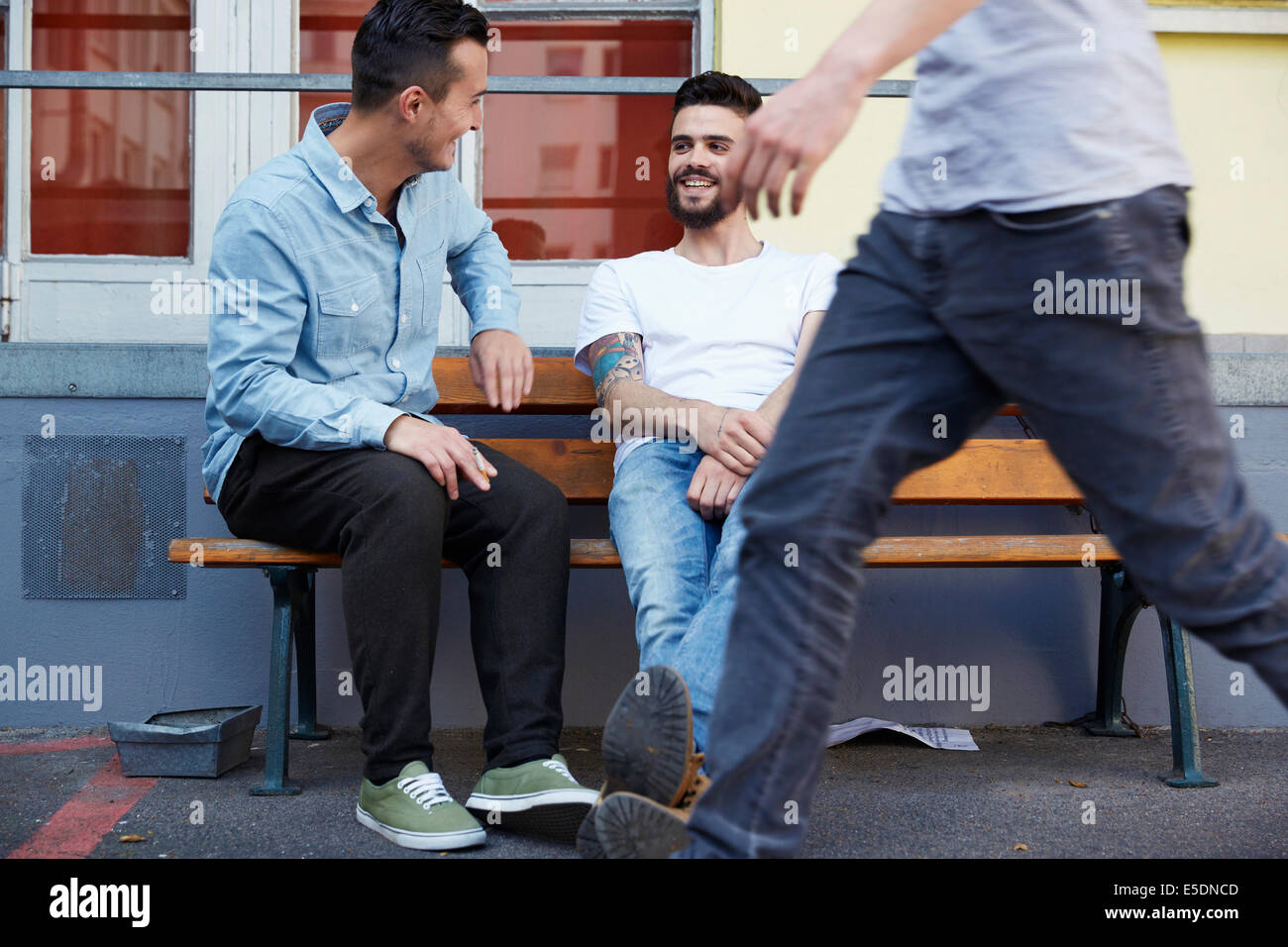 Two men sitting on bench with person passing by Stock Photo - Alamy