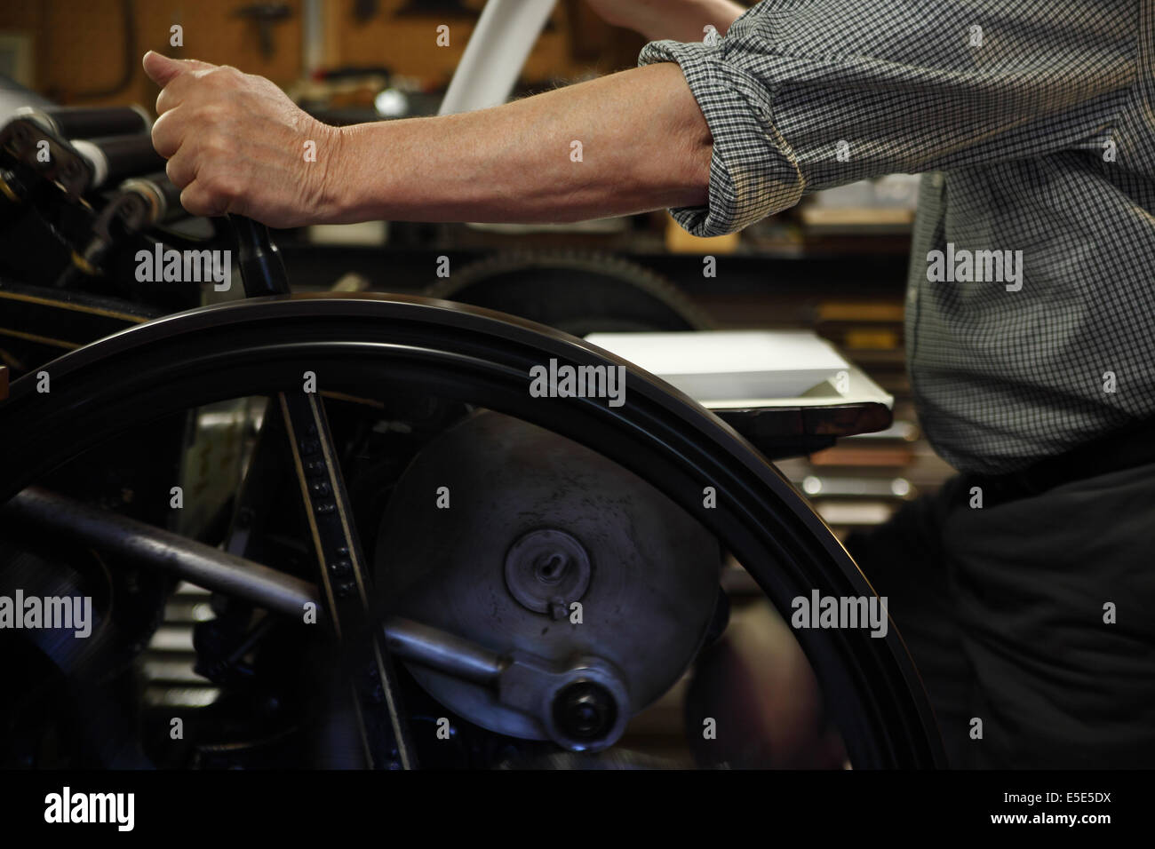 A printer works the flywheel of an antique letterpress machine in his ...