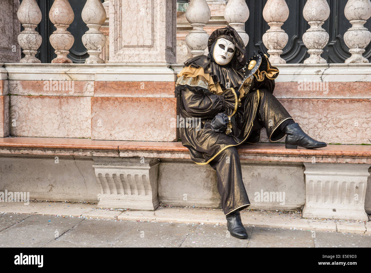 Man in stylized black and gold Carnival jester's costume sits outside ...