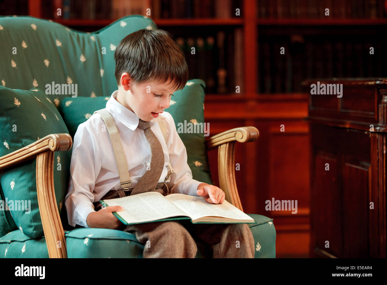Cute little boy reading book on armchair Stock Photo - Alamy