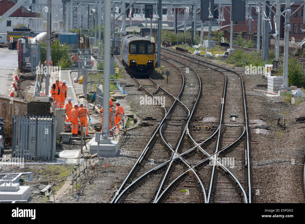 Railway workmen in orange overalls work beside the tracks while a train ...