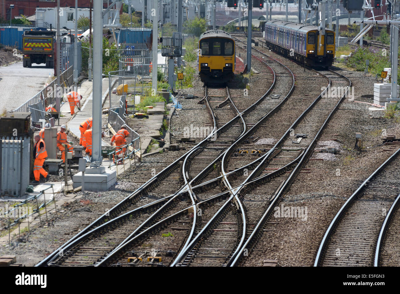 Railway workmen in orange overalls work beside the tracks while a train ...