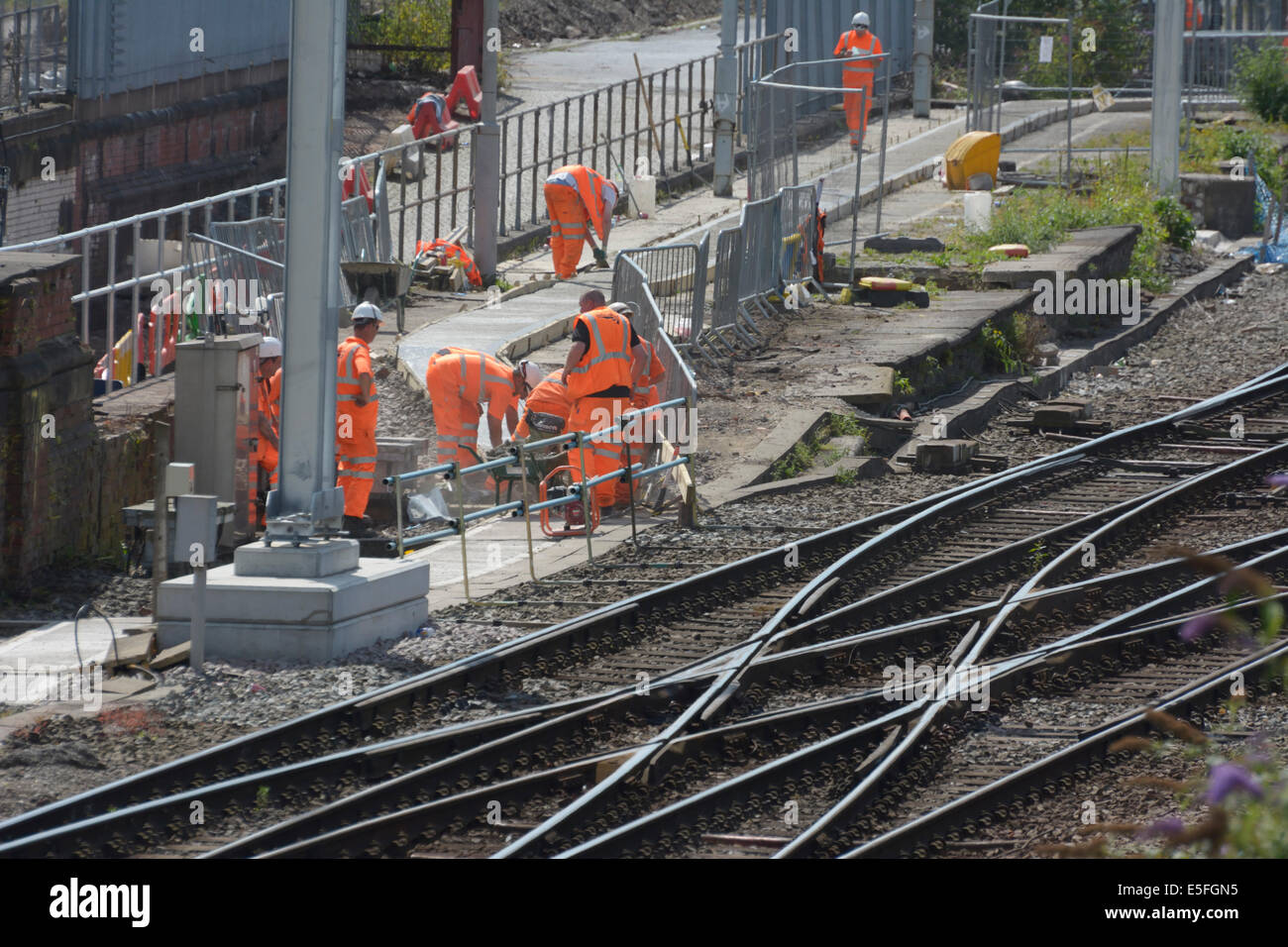 Railway workmen in orange overalls work beside the tracks while a train ...