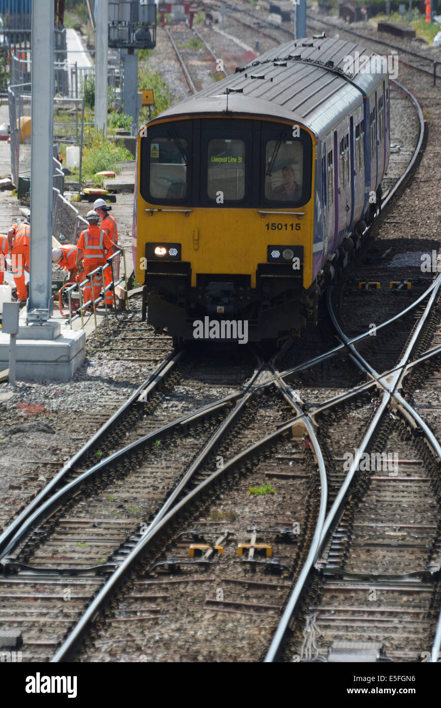 Railway workmen in orange overalls work beside the tracks while a train ...