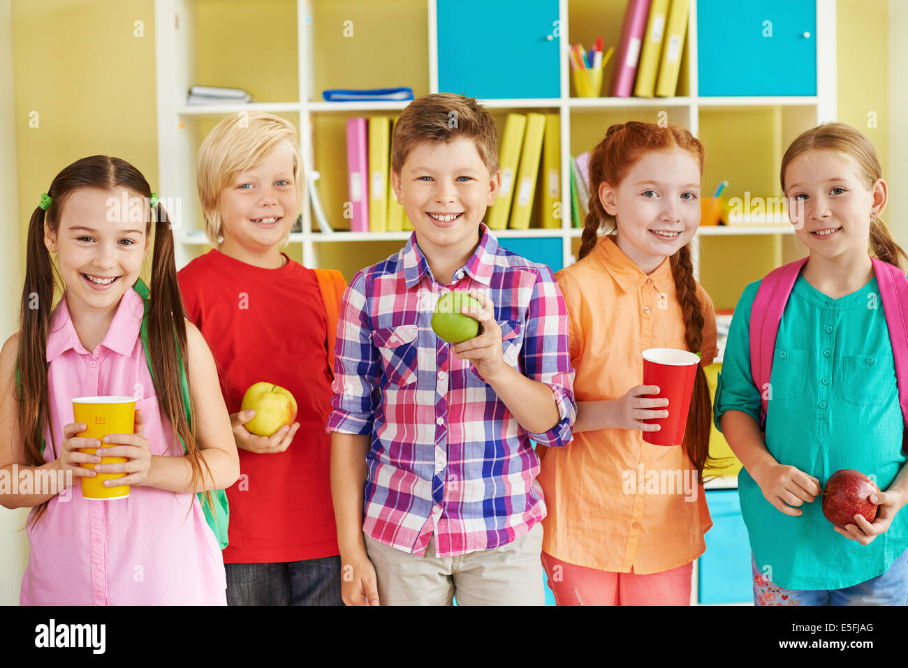 Portrait of friendly classmates with drinks and green apples looking at ...