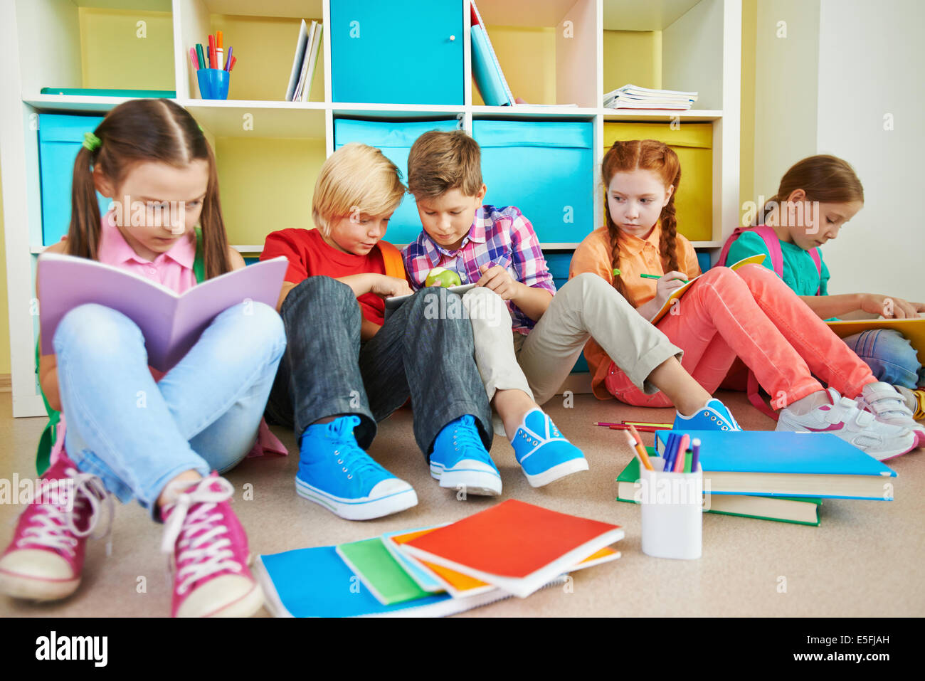 Portrait of friendly classmates sitting on the floor of classroom and ...