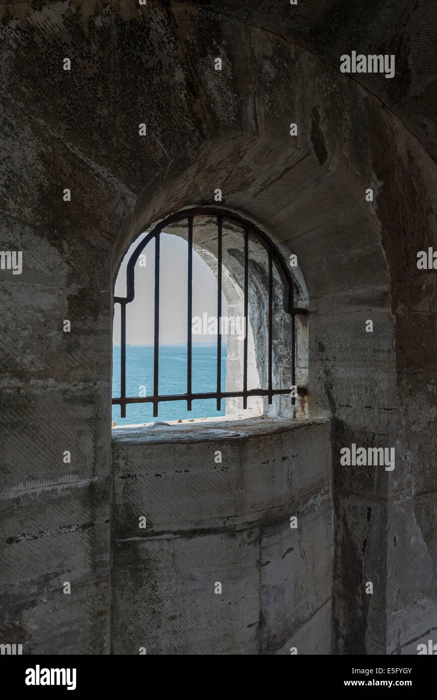 A stone arched window covered with steel bars looking out to a view at ...