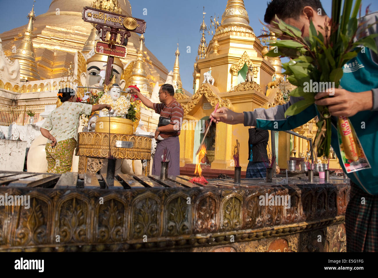 A man lights an incense offering at the Tuesday Corner of the Shewdagon ...