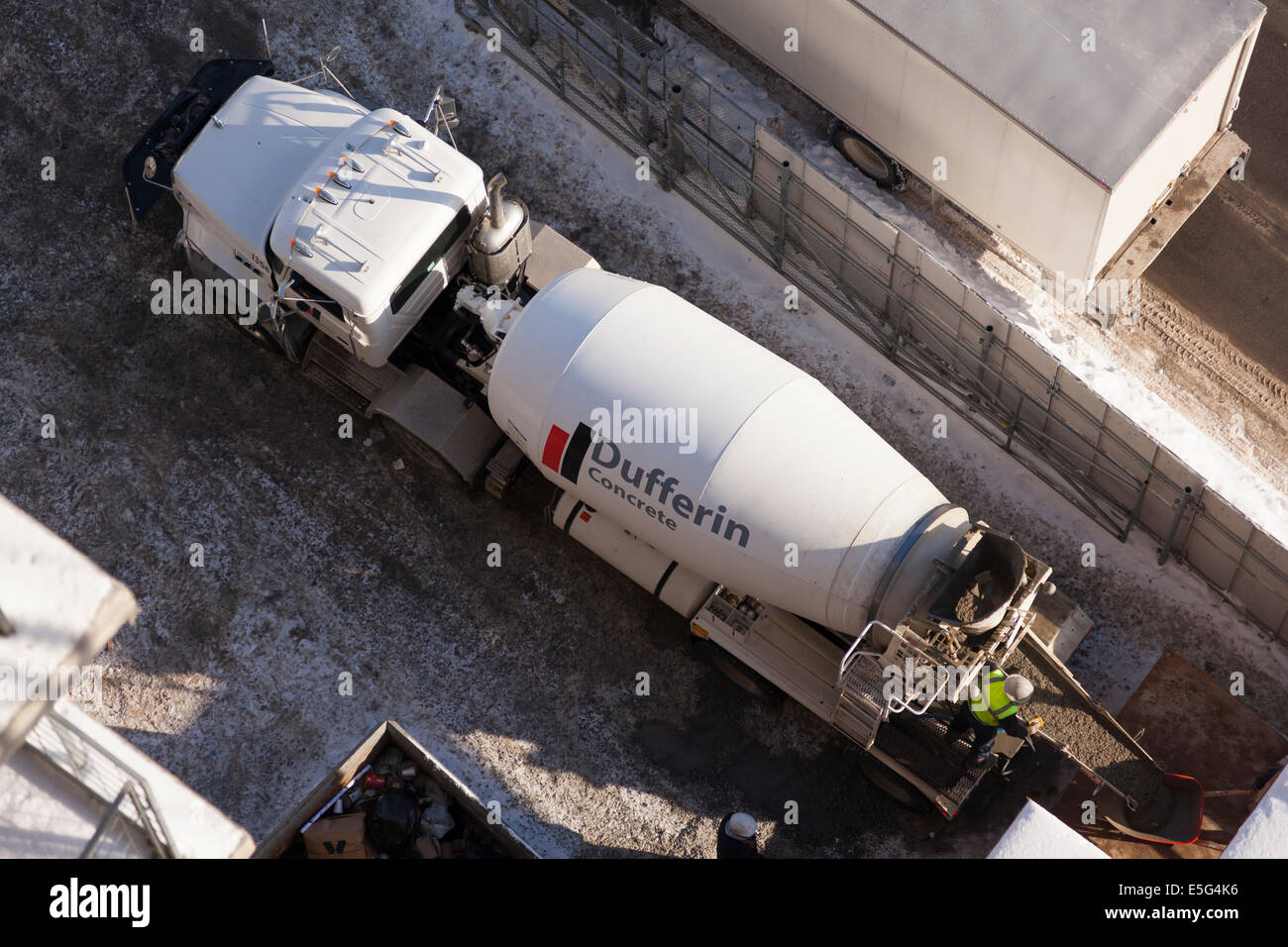 A cement mixer truck dumping a load of fresh concrete with a worker ...
