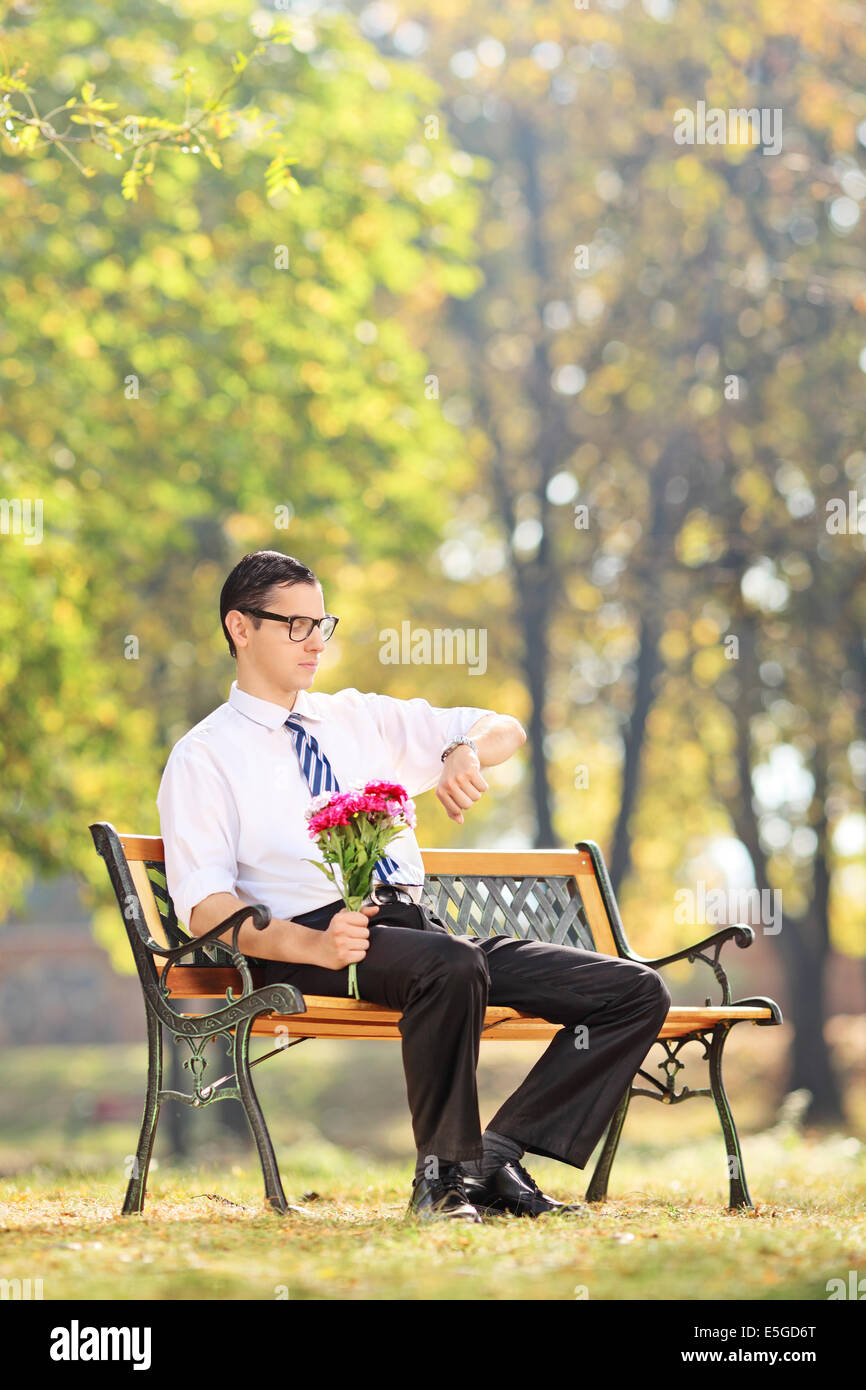 Vertical shot of a young guy waiting for his date seated on bench in ...