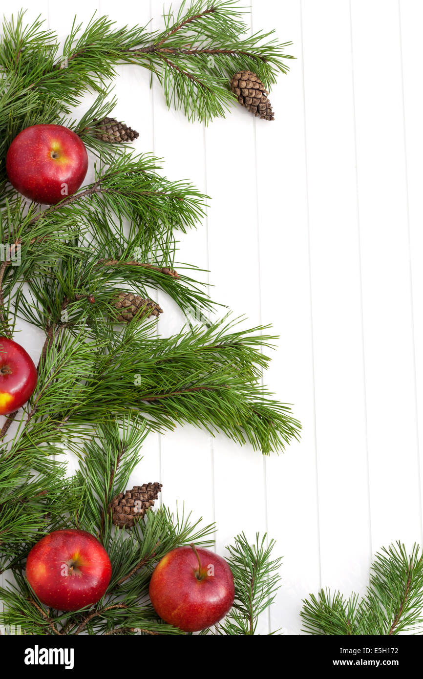 Decorated pine branches with cones and red apples on white wooden table ...