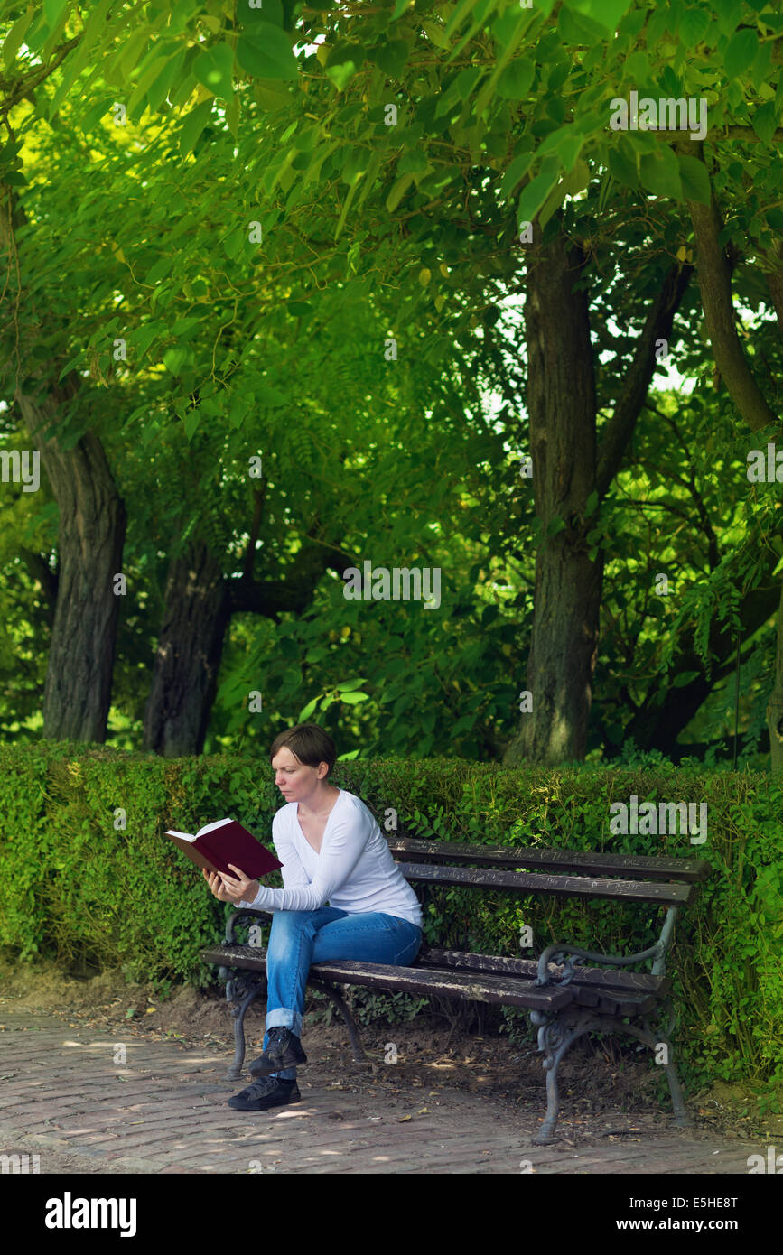 Beautiful young adult woman reading hardcover book while sitting on a ...