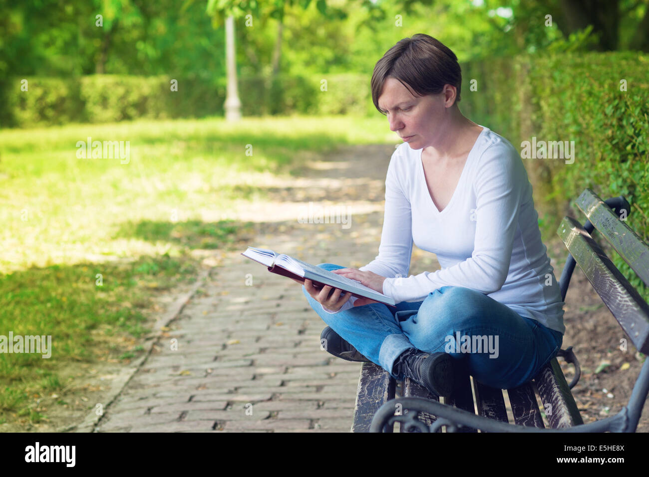 Beautiful young adult woman reading hardcover book while sitting on a ...