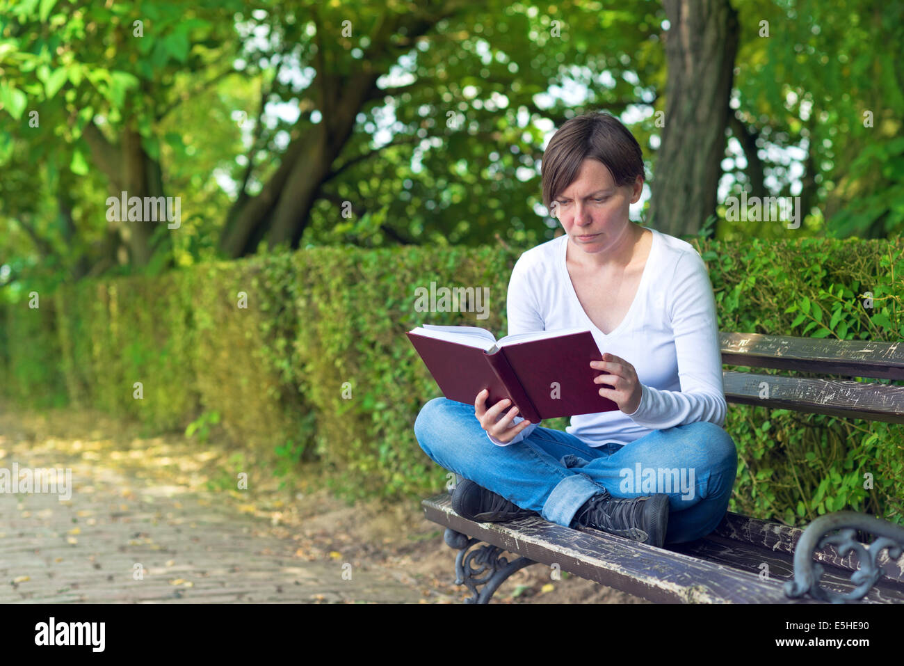 Beautiful young adult woman reading hardcover book while sitting on a ...