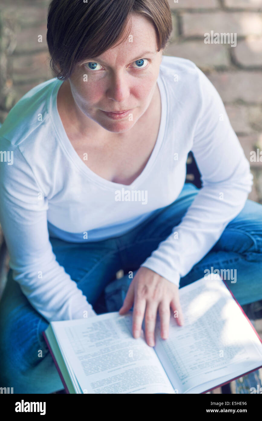 Beautiful young adult woman reading hardcover book while sitting on a ...