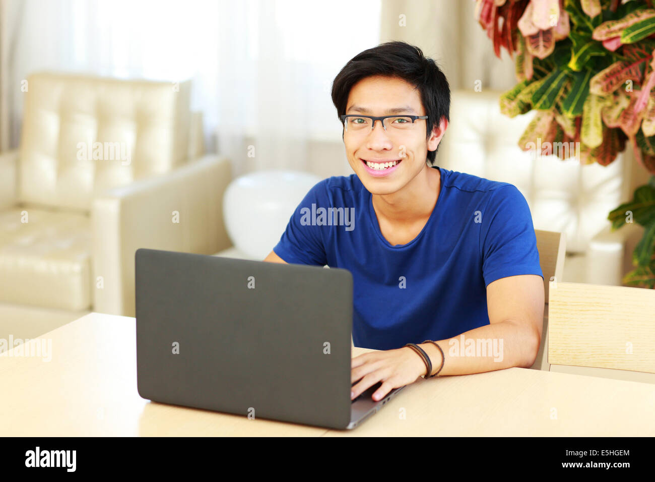 Smiling asian man sitting at the table with laptop Stock Photo - Alamy