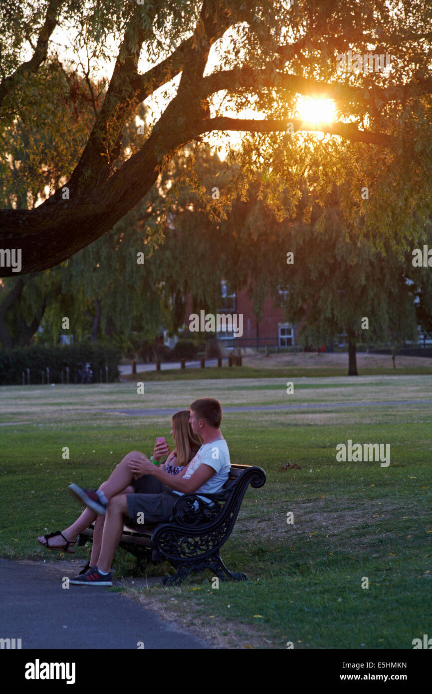 couple sat on bench in park at Christchurch, Dorset as the sun goes ...