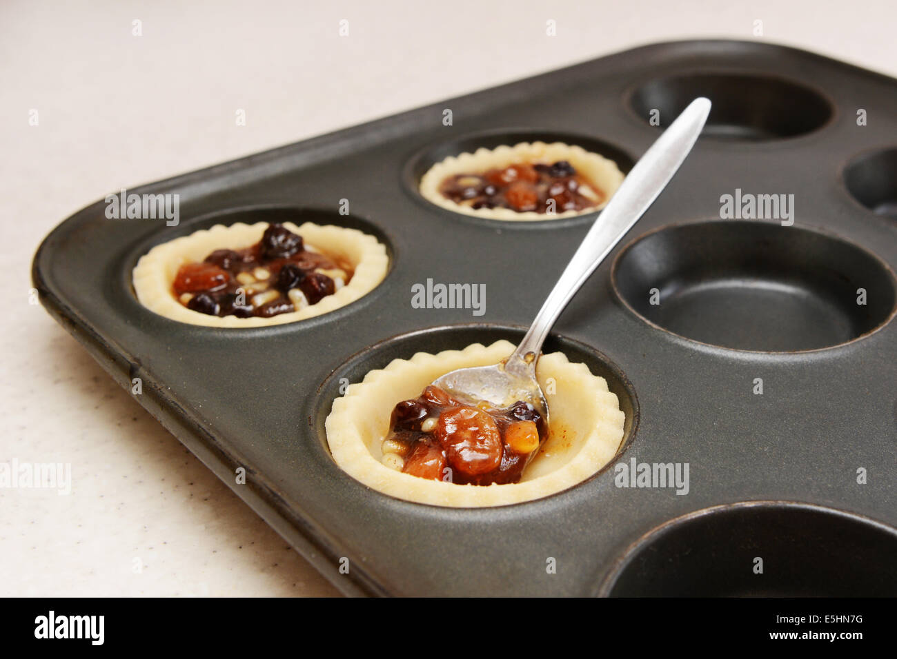 Spooning mincemeat into pastry cases in a bun tin with a teaspoon Stock ...