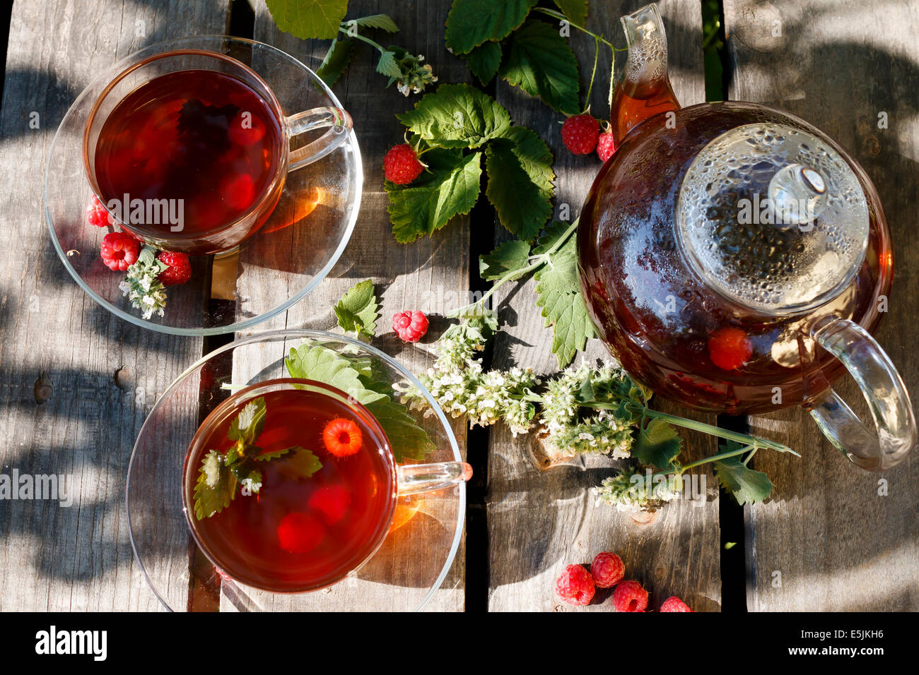 raspberry tea in transparent teapot and teacups on wooden table at ...